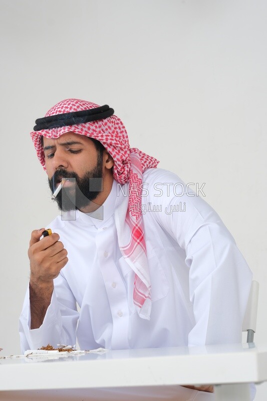 Saudi man wearing a white thobe and shemagh takes a deep breath from a ...